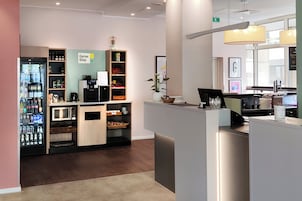 Um saguão moderno de hotel com balcão de recepção, minibar e placa da 'Garnier Shop'.