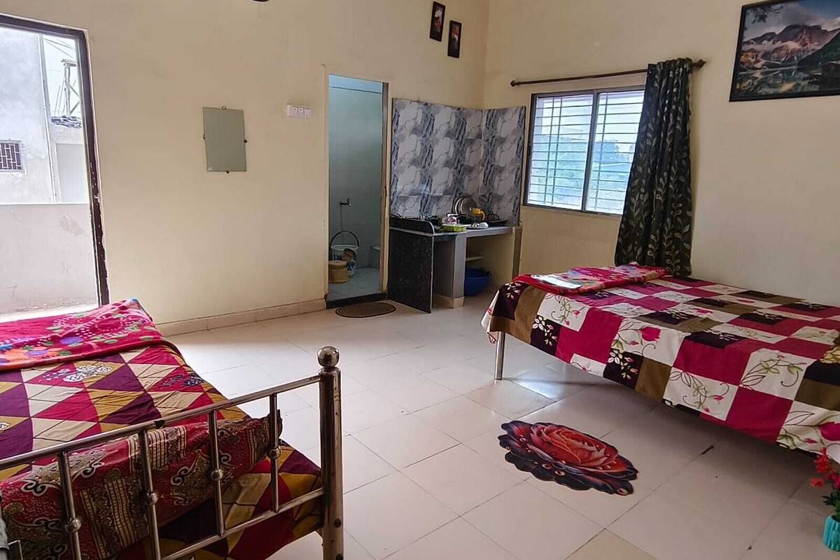 Quarto com duas camas, uma escrivaninha, uma cadeira, uma janela com cortinas e um ventilador de teto.