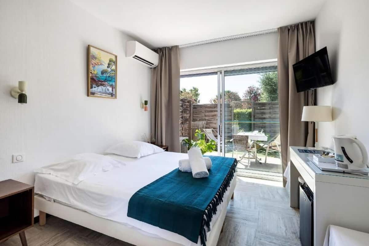 Quarto de hotel com cama, escrivaninha, televisão e varanda com mesa e cadeiras.