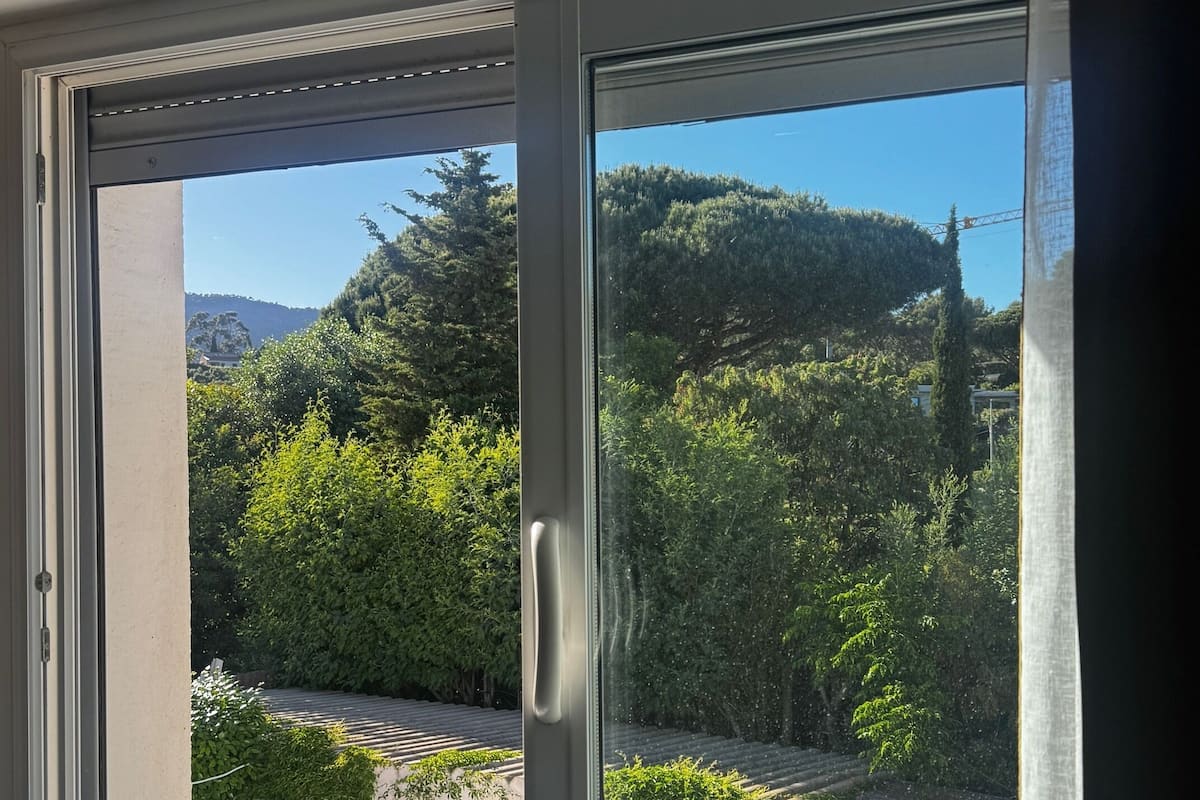 Janela com vista para uma paisagem verde, incluindo árvores e uma colina.