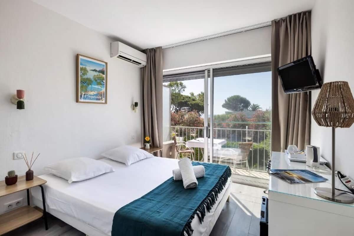 Quarto de hotel com cama, escrivaninha, cadeira, televisão e varanda com vista.
