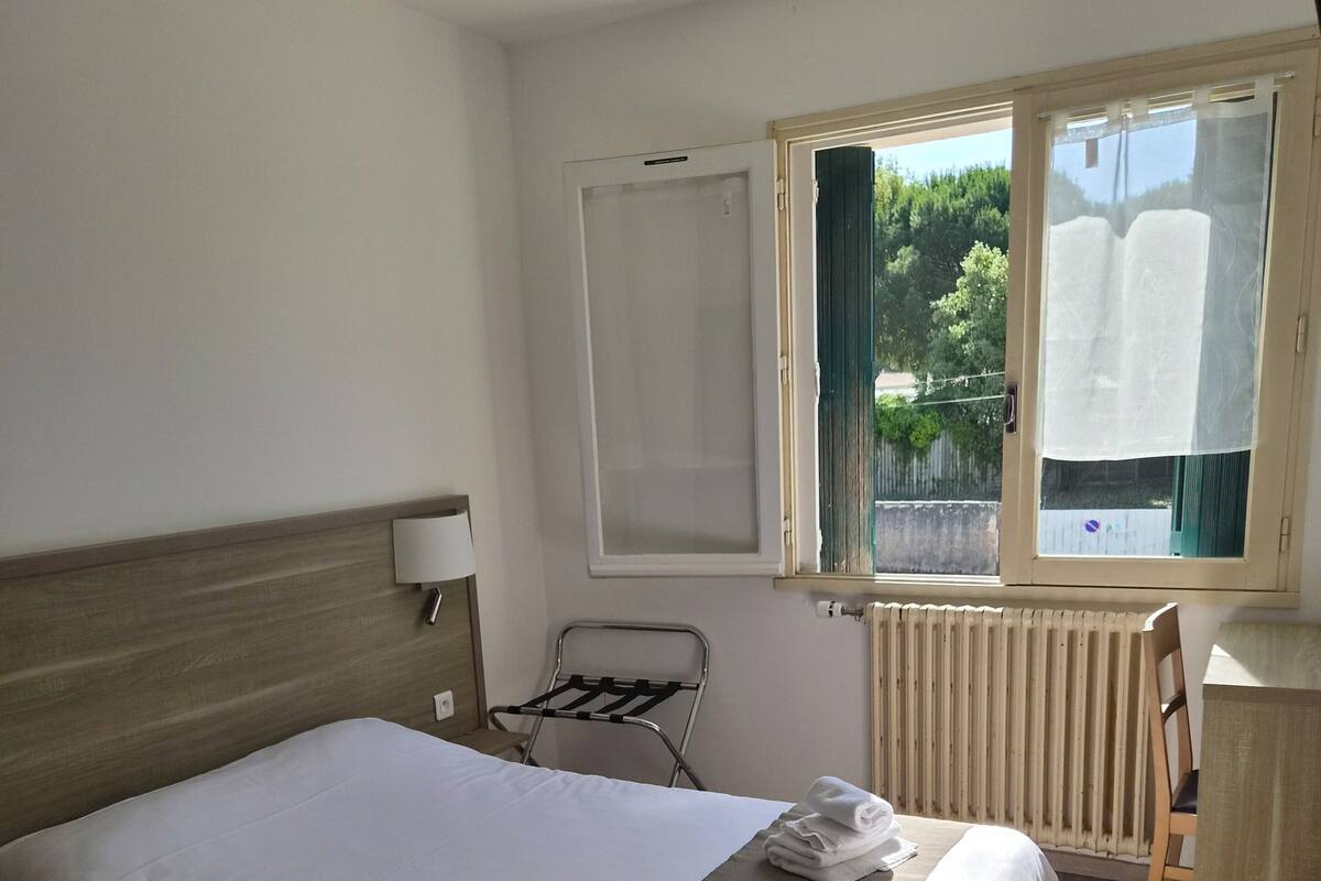 Quarto de hotel com cama, janela com vista, radiador e escrivaninha.