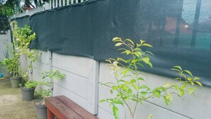Paredes de concreto com tela verde de malha, um banco de madeira e plantas em vasos.