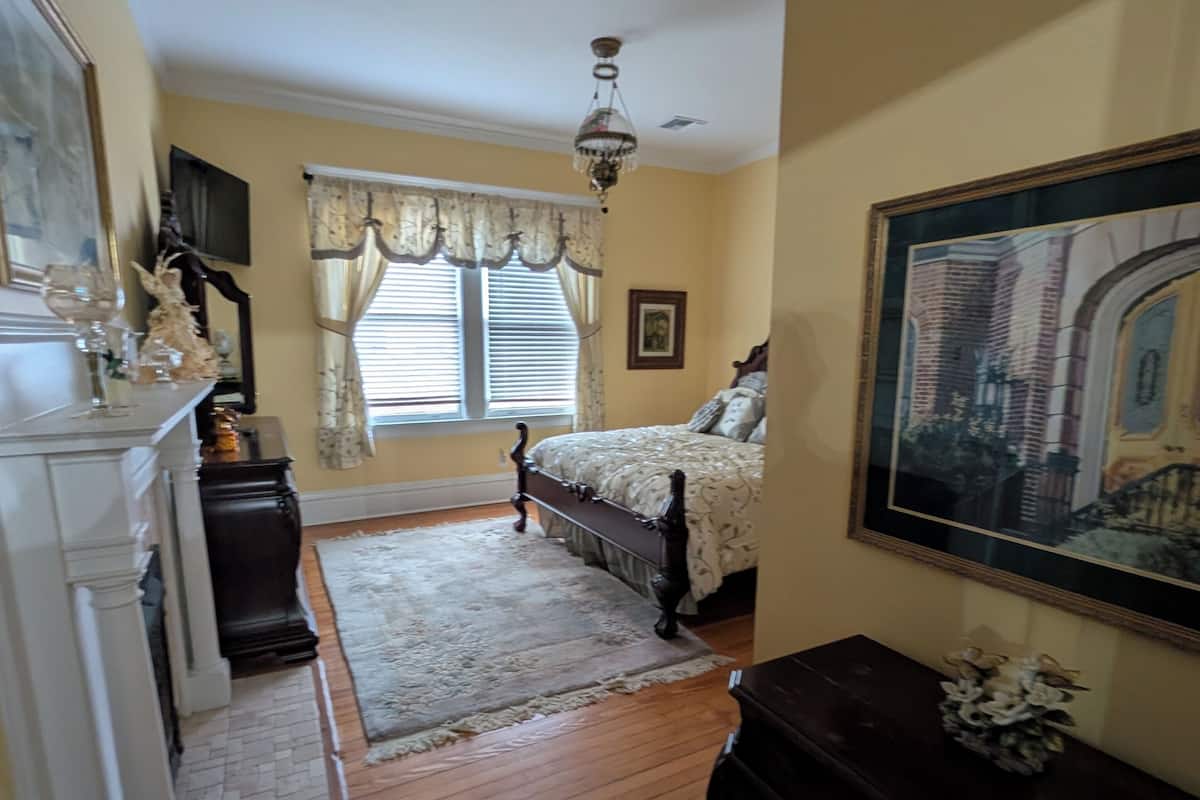 Um quarto com cama, cômoda, espelho, lustre e um quadro na parede.