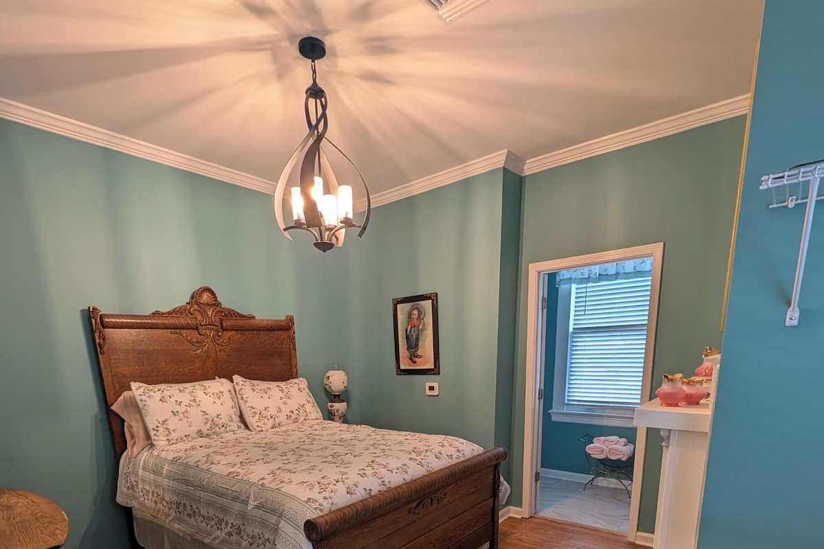 Um quarto com cama de madeira, um candelabro, um quadro na parede e uma cômoda com design floral.