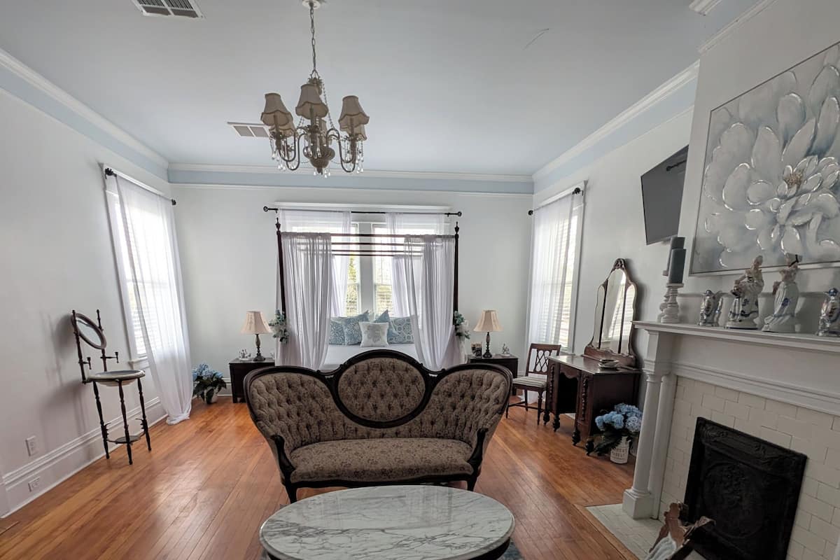 Uma sala de estar com sofá, duas poltronas, mesa de centro, lareira e um grande quadro floral na parede.