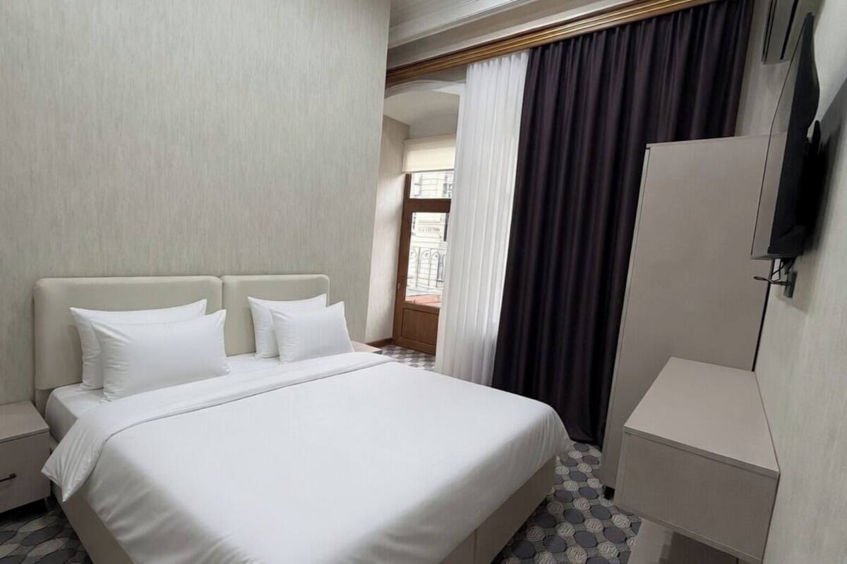Quarto de hotel com cama, guarda-roupa, mesa de cabeceira e vista para o exterior.