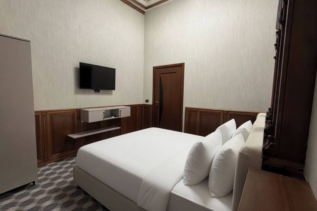 Quarto de hotel com cama, televisão, guarda-roupa e secretária.