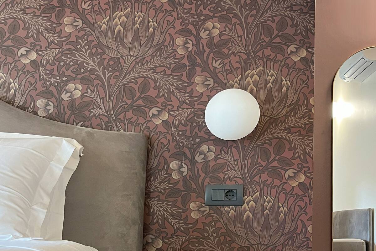 Quarto com cama, luminária na parede e tomada.