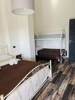 Quarto com uma cama de solteiro, mesa de cabeceira com luminária e piso de madeira.