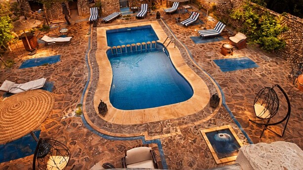 Uma área de piscina com espreguiçadeiras e guarda-sóis, cercada por muros de pedra e vegetação.