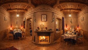 Uma sala de jantar acolhedora com lareira, vigas de madeira e piso de azulejos.