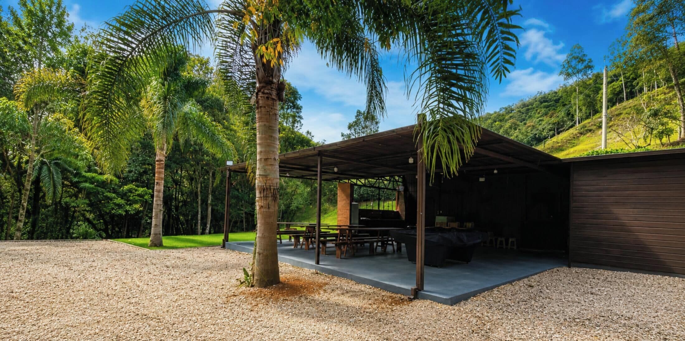 Um espaço ao ar livre coberto com mesas de piquenique e um piano, cercado por árvores e uma colina gramada.