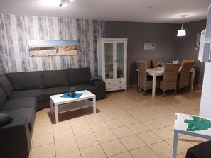 Uma sala de estar com sofá, mesa de centro, armário e um espaço de jantar com cadeiras.