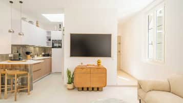 Cozinha moderna com área de jantar, televisão de tela plana na parede e um espaço de estar com sofá.
