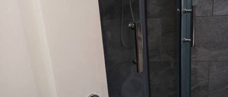 Um chuveiro com divisória de vidro, porta branca e puxador de metal.