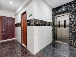 Um hall com porta de madeira, sinal de saída de incêndio e elevador com visor digital.