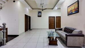 Um hall amplo com um sofá, uma mesa de centro de vidro, um ventilador de teto e uma pintura na parede.