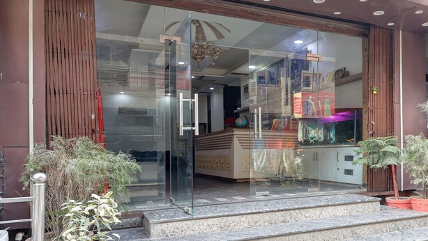 Entrada de hotel com porta de vidro, balcão de recepção e escada que dá acesso ao interior.