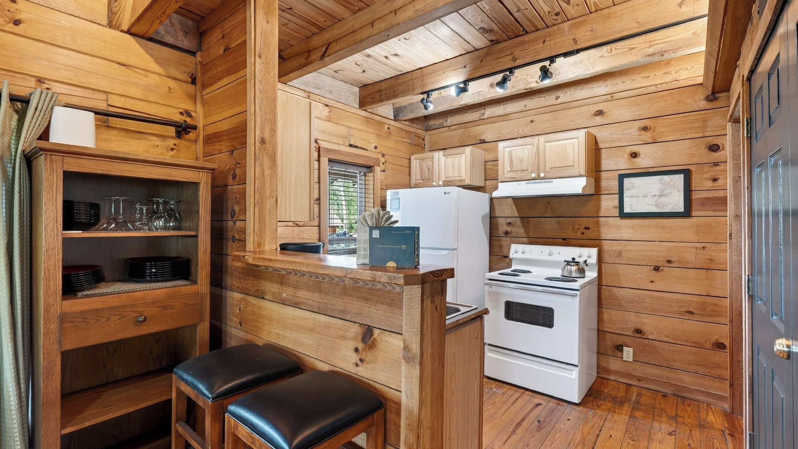 Interior de uma cabana de madeira, com cozinha equipada, incluindo fogão, geladeira e armários de madeira.