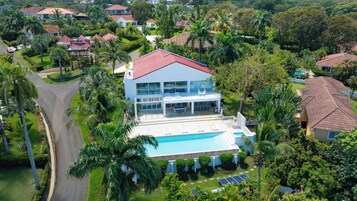 Uma casa moderna de dois andares com piscina, rodeada por vegetação exuberante e palmeiras.