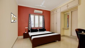 Quarto com cama, mesa de cabeceira, cadeira, guarda-roupa e ventoinha no teto.