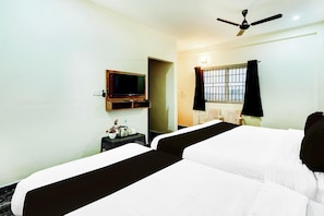Quarto de hotel com duas camas, uma televisão, ventilador de teto, janela com cortinas e uma pequena mesa com uma planta.