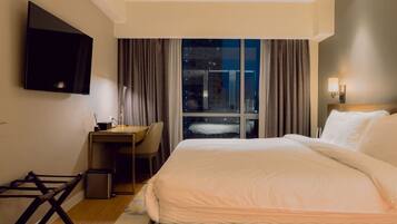 Quarto de hotel com cama, secretária, televisão e janela com cortinas.