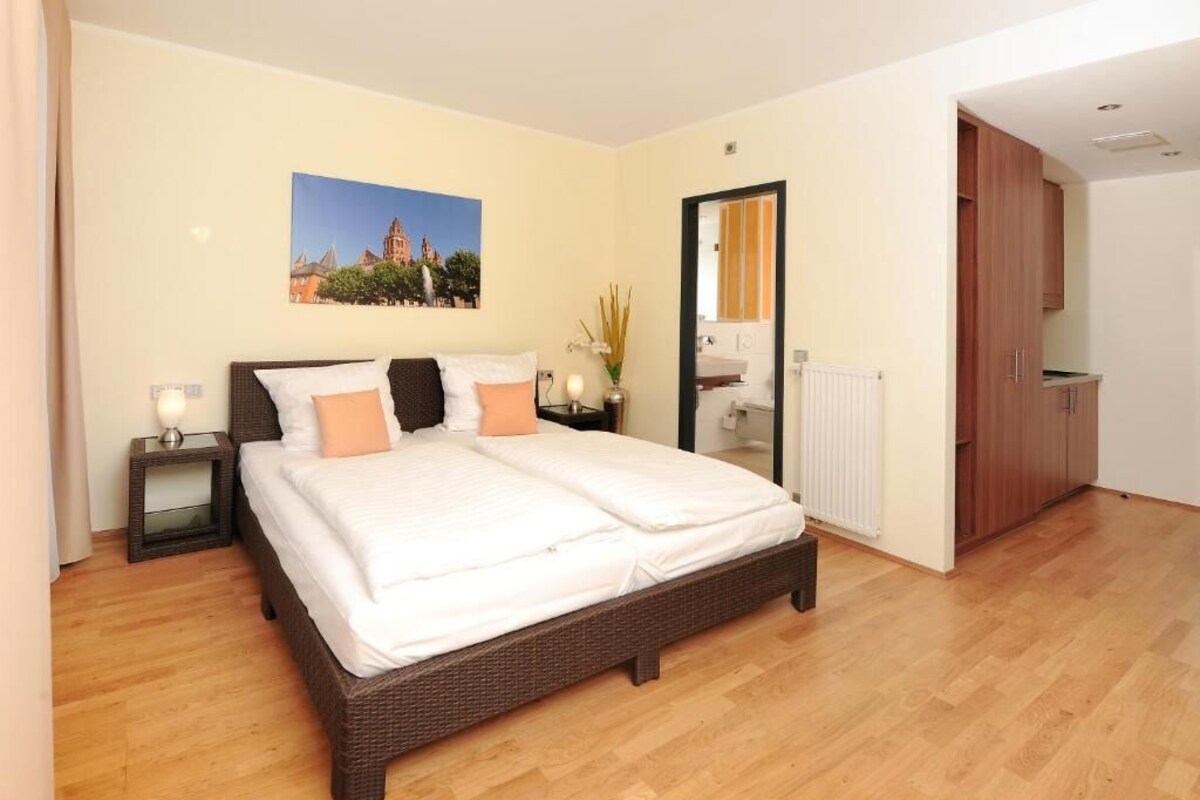 Quarto com uma cama grande, mesa de cabeceira, espelho, radiador e guarda-roupa.