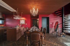 Uma sala de jantar com mesa de madeira, cadeiras, um candelabro e uma escada.