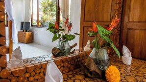 Um banheiro com piso de madeira, um espelho, uma pia com um vaso de flores e uma toalha no balcão.