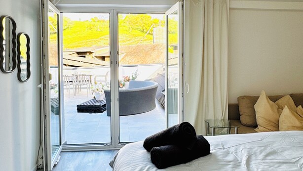 Quarto de hotel com cama, sofá, mesa pequena e porta de vidro deslizante para área externa com varanda e banheira de hidromassagem.
