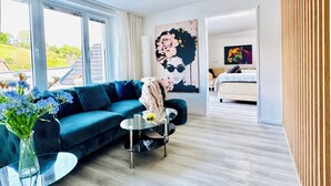 Uma sala de estar moderna com um sofá azul, uma mesa de centro de vidro e uma pintura na parede.