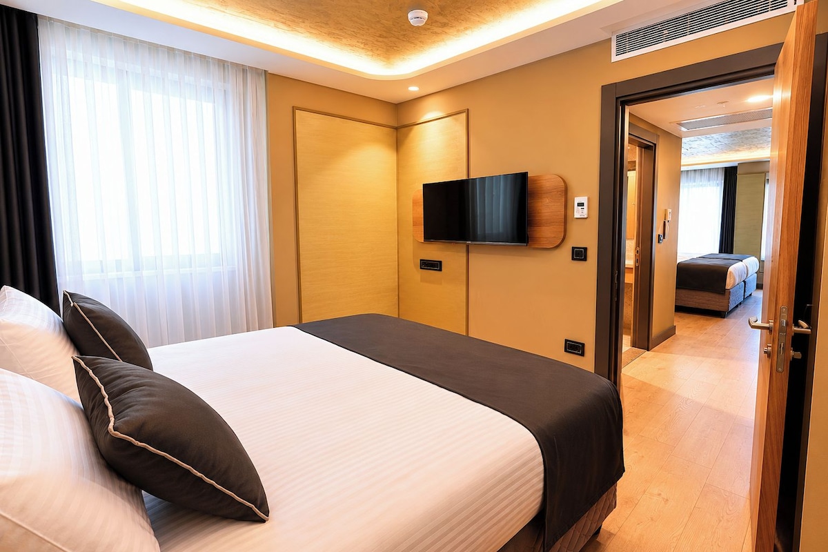 Quarto de hotel com uma cama, uma televisão presa na parede e uma porta que dá para outro espaço.