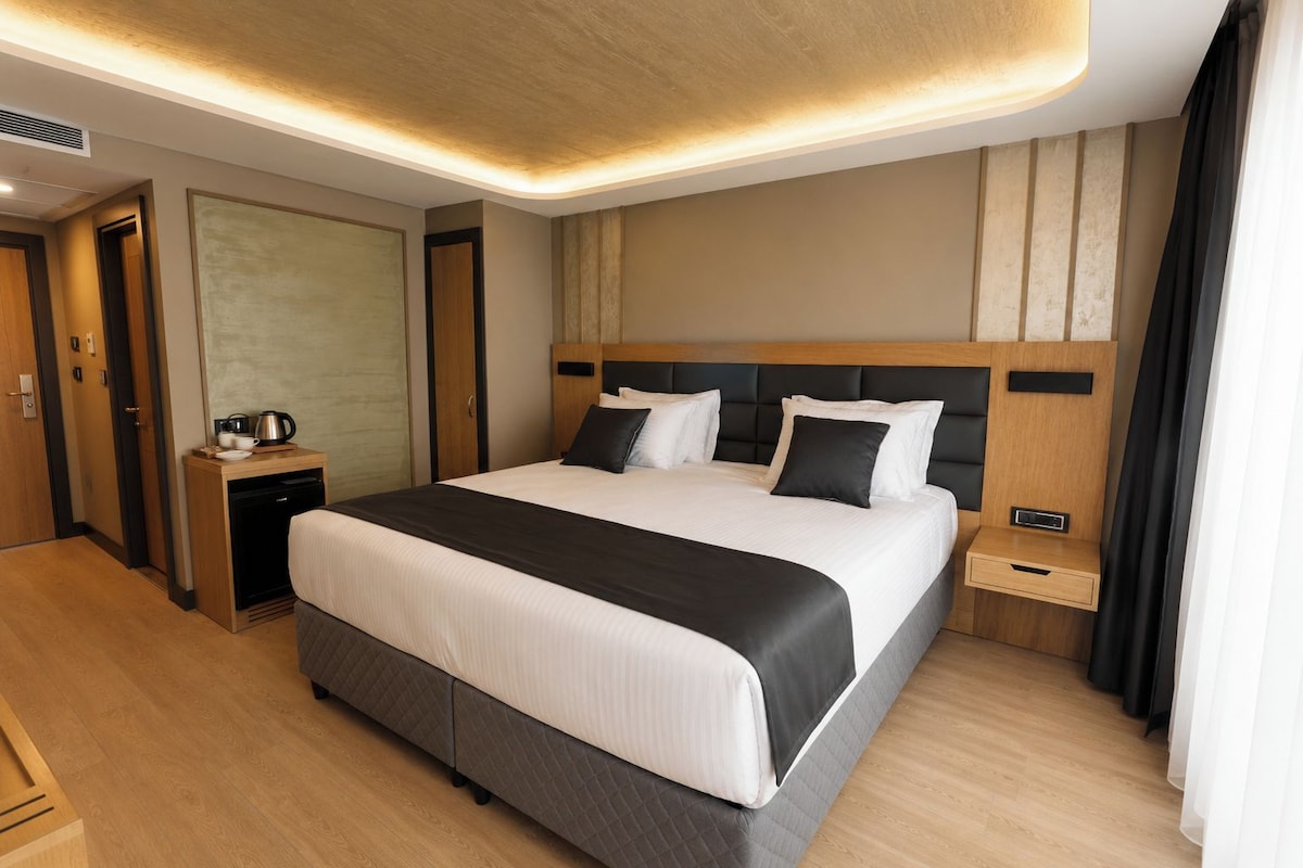 Quarto de hotel moderno com uma cama grande, mesas de cabeceira, aquecimento integrado e vista para a cidade.