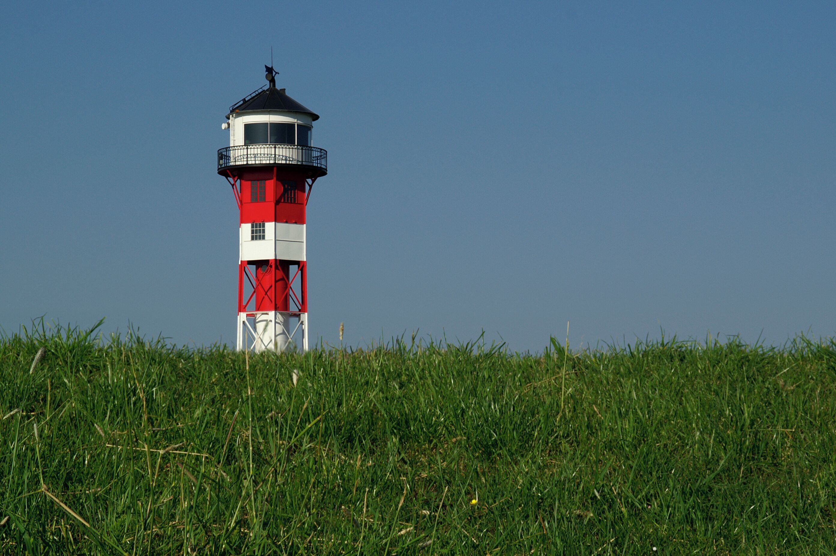 Um farol com uma torre listrada de vermelho e branco, rodeado por grama.