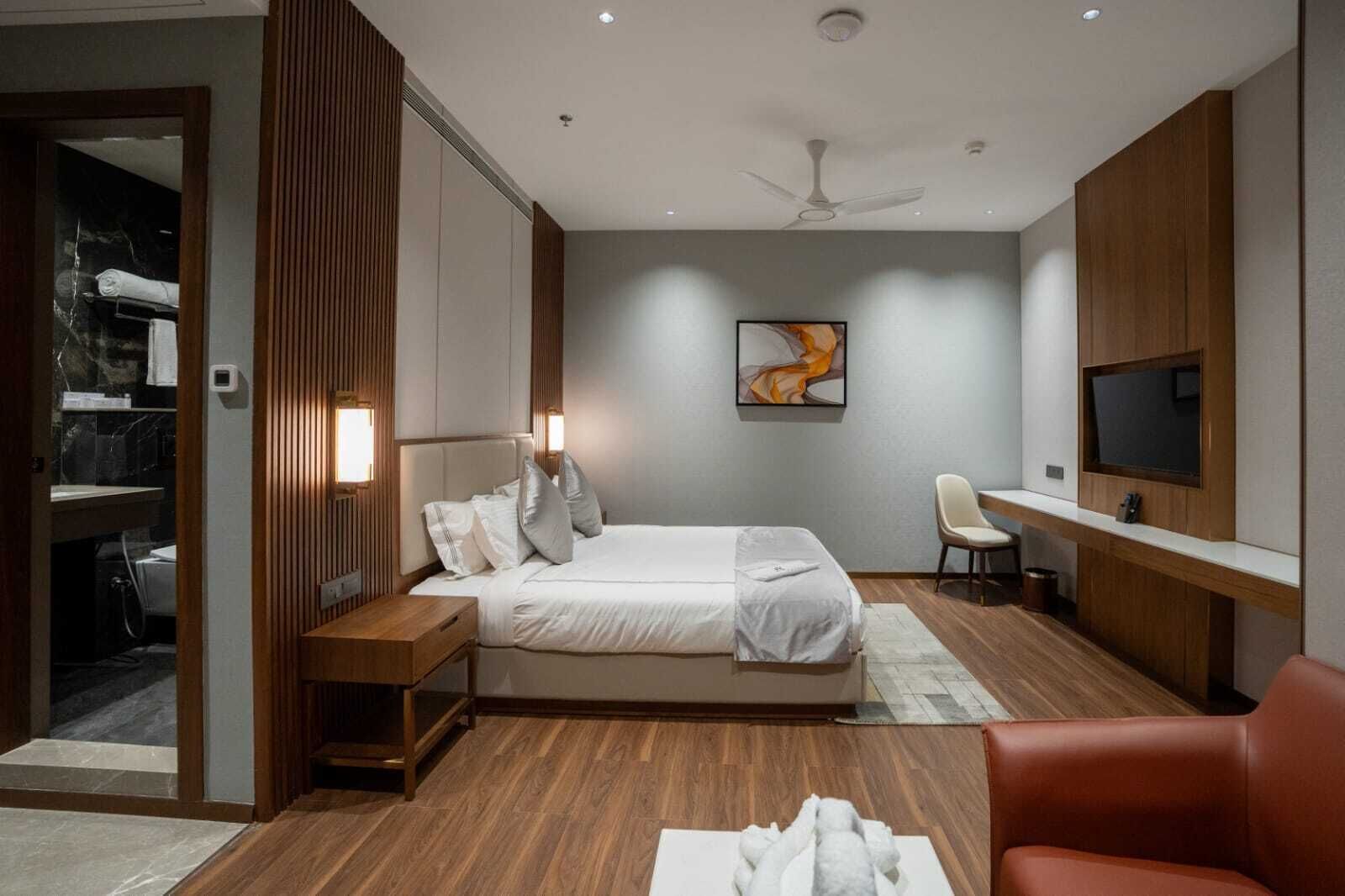 Quarto de hotel moderno com cama, mesa de cabeceira, televisão e um espaço de estar.
