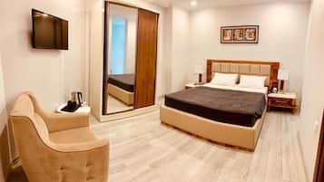 Quarto de hotel com cama, poltrona, televisão, mesa de cabeceira e um espelho grande.