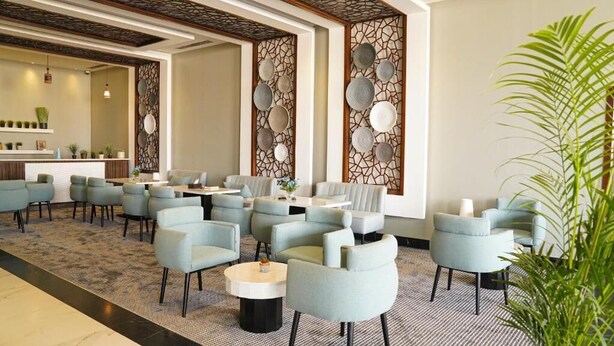 Um saguão de hotel com disposição de assentos, balcão de recepção, painéis decorativos na parede e um vaso de planta.