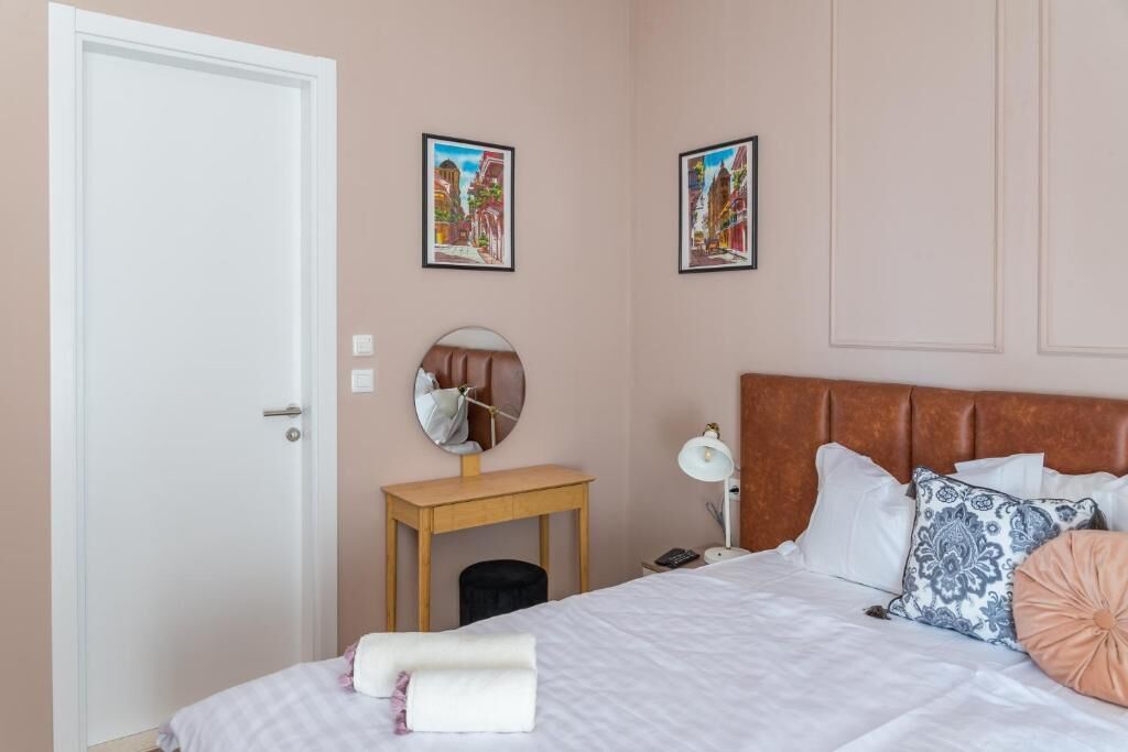 Um quarto com cama, mesa de cabeceira, espelho, luminária e duas molduras na parede.