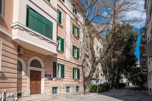 Um edifício de vários andares com fachada de pedra, persianas verdes e uma entrada central com porta.