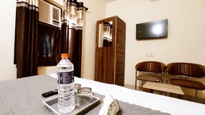 Quarto de hotel com cama, garrafa de água, controle remoto, bandeja, lenço de papel e televisão na parede.