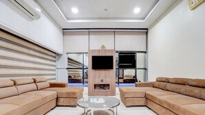 Uma sala de estar moderna com um sofá seccional, uma mesa de centro, uma televisão fixada em um móvel de madeira e grandes janelas.