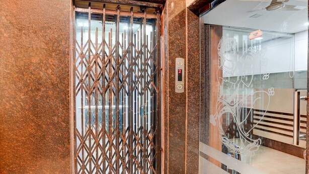 Um elevador com portão de segurança metálico, visor digital e porta de vidro com design decorativo.