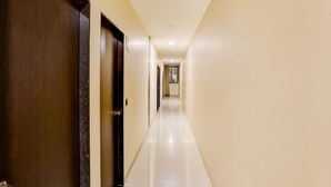 Um corredor de hotel comprido e estreito, com portas de um lado e uma parede lisa do outro.