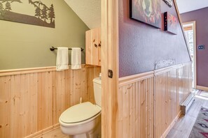 Casa de banho com painéis de madeira, vaso sanitário, toalhas e um quadro na parede.