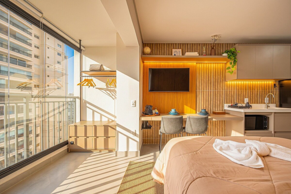 Quarto moderno com uma cama grande, uma escrivaninha e vista para o horizonte urbano através de janelas do chão ao teto.