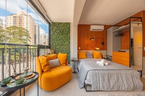 Quarto de hotel moderno com varanda, uma cama com edredom cinza, sofá amarelo e parede verde.