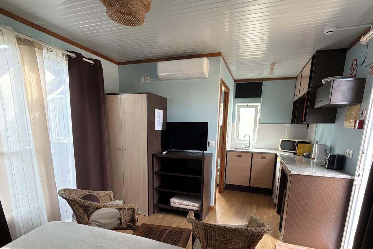 Quarto compacto com cama, televisão, cozinha compacta e móveis de vime.