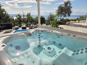 Uma banheira de hidromassagem com vista para o mar, cercada por espreguiçadeiras e um deck de madeira.